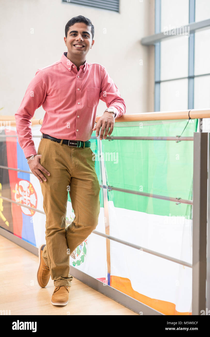 a male confident international student stands on campus with flags ...