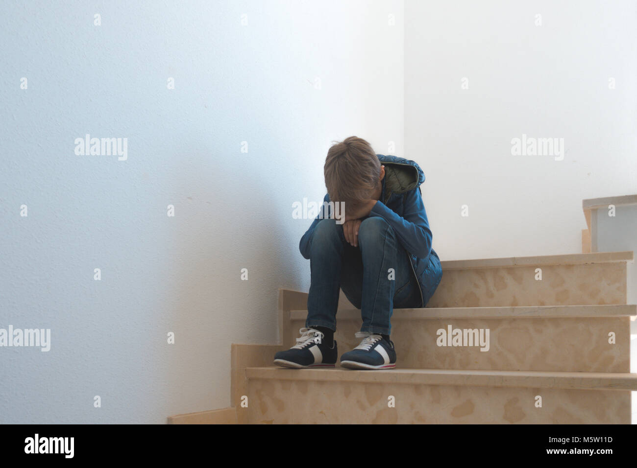 Sad boy sitting alone in the corner in the staircase Stock Photo - Alamy