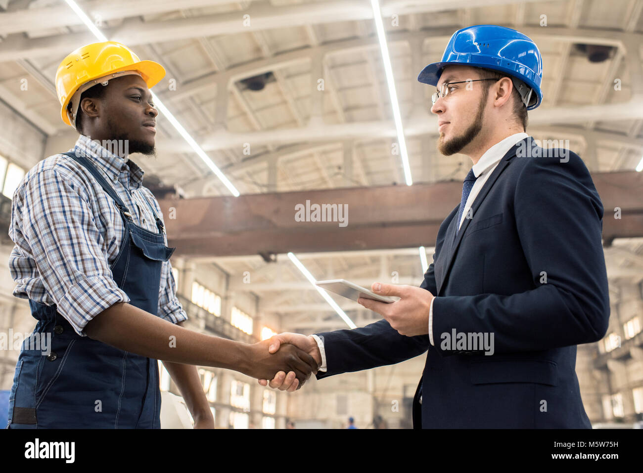 Handsome African American worker wearing overall and hardhat greeting ...