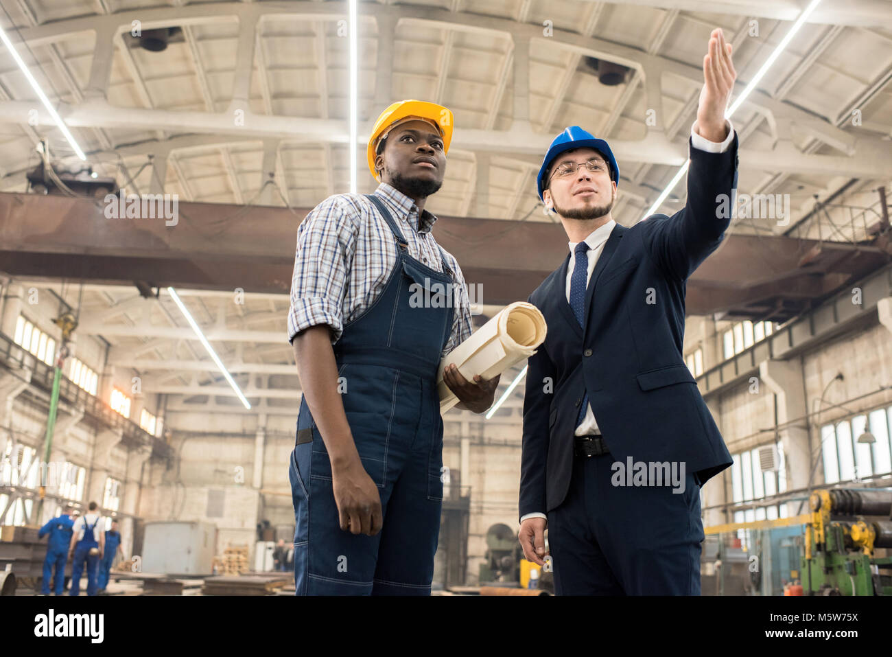 Confident inspector in classical suit pointing at something while young ...