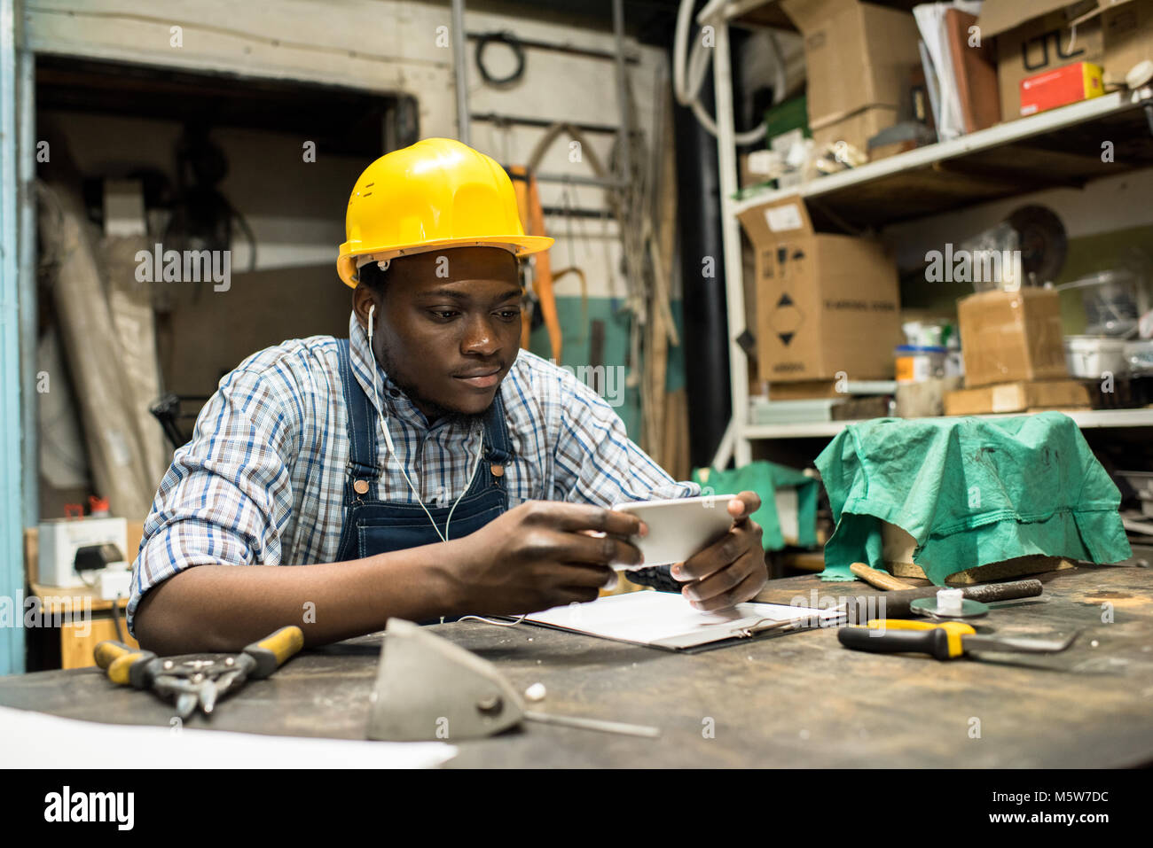 Concentrated African American lathe operator sitting at work bench and ...