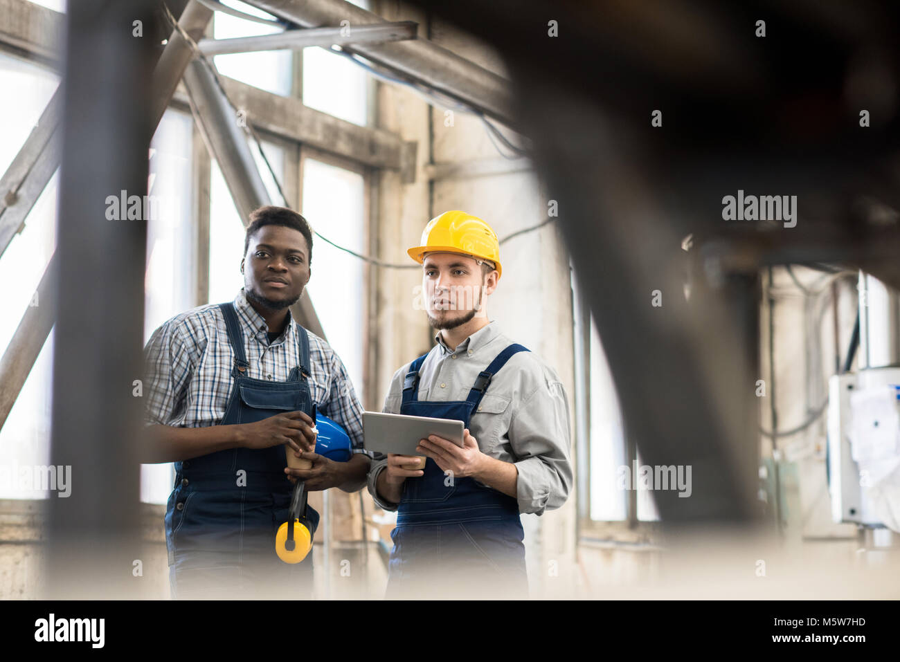 Multi-ethnic group of machine operators wearing overalls looking away ...