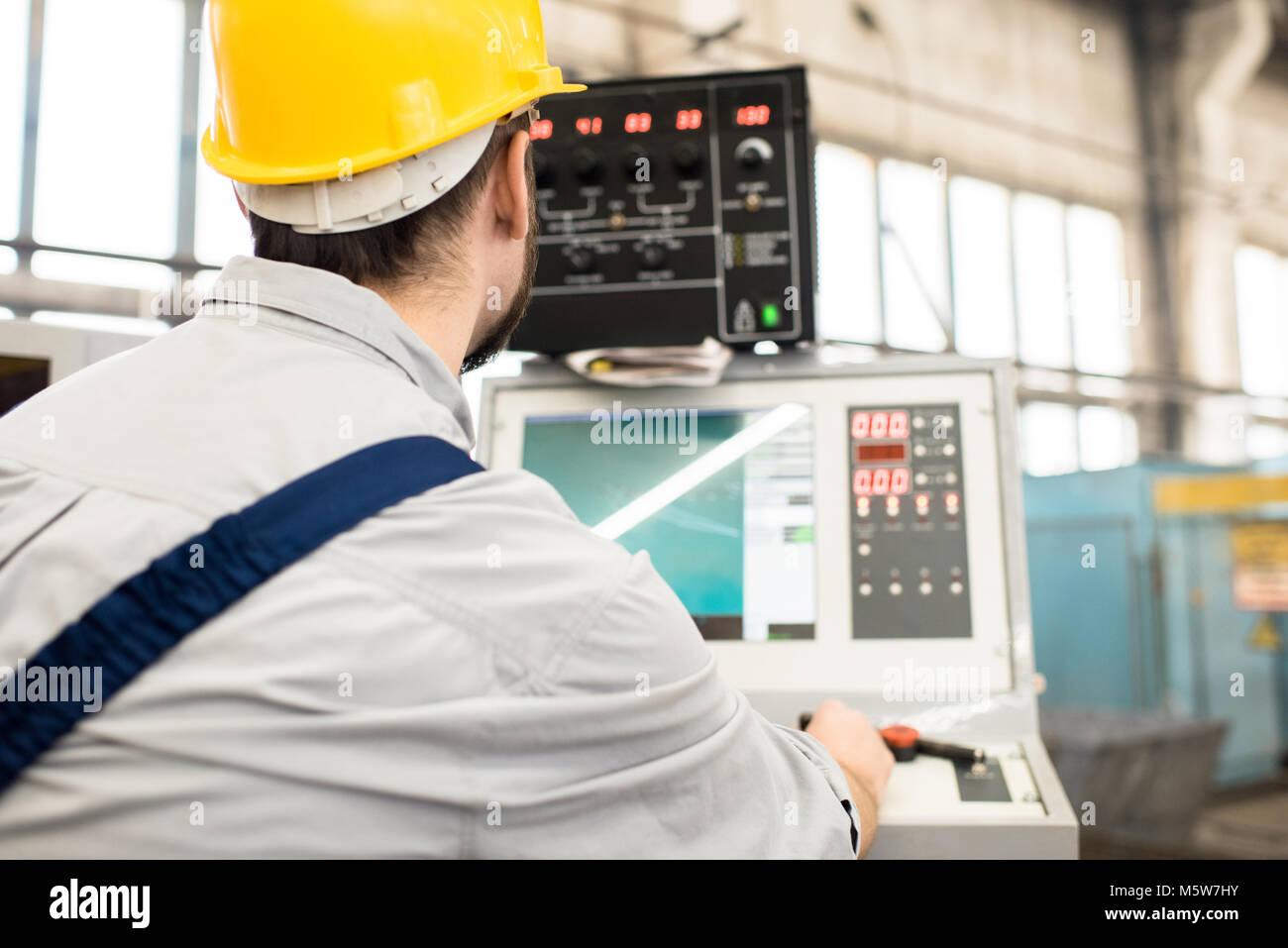 Back view of bearded operator wearing protective helmet focused on work ...