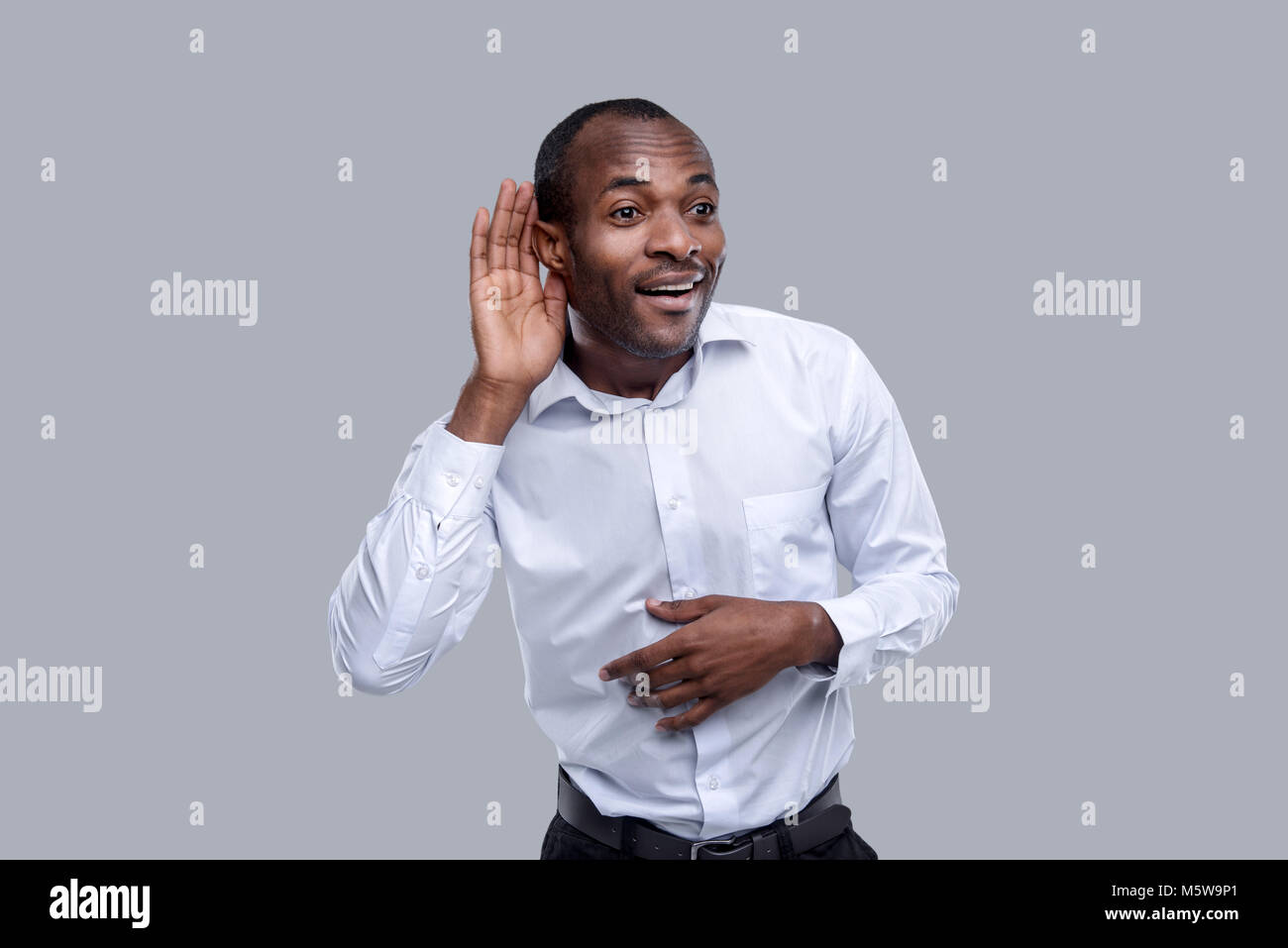 Glad afro-american man having his hand hear his ear Stock Photo - Alamy