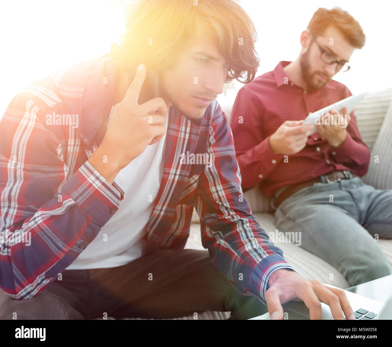 two guys sitting on the couch, talking on the smartphone and ...