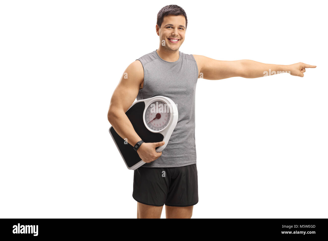 Young man in sportswear holding a weight scale and pointing isolated on ...