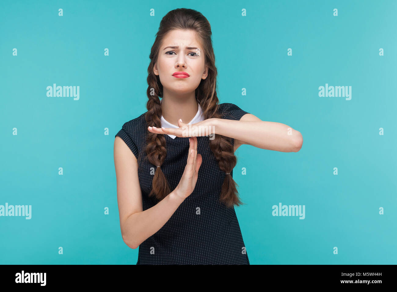 Well dressed woman showing time out sign at camera. Studio shot, blue ...