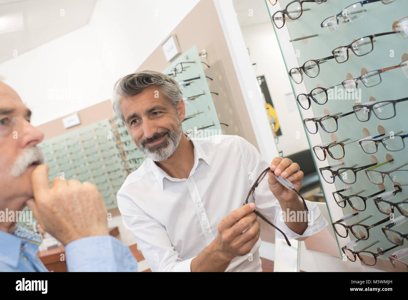 male optician consulting adult customer near glasses display Stock ...