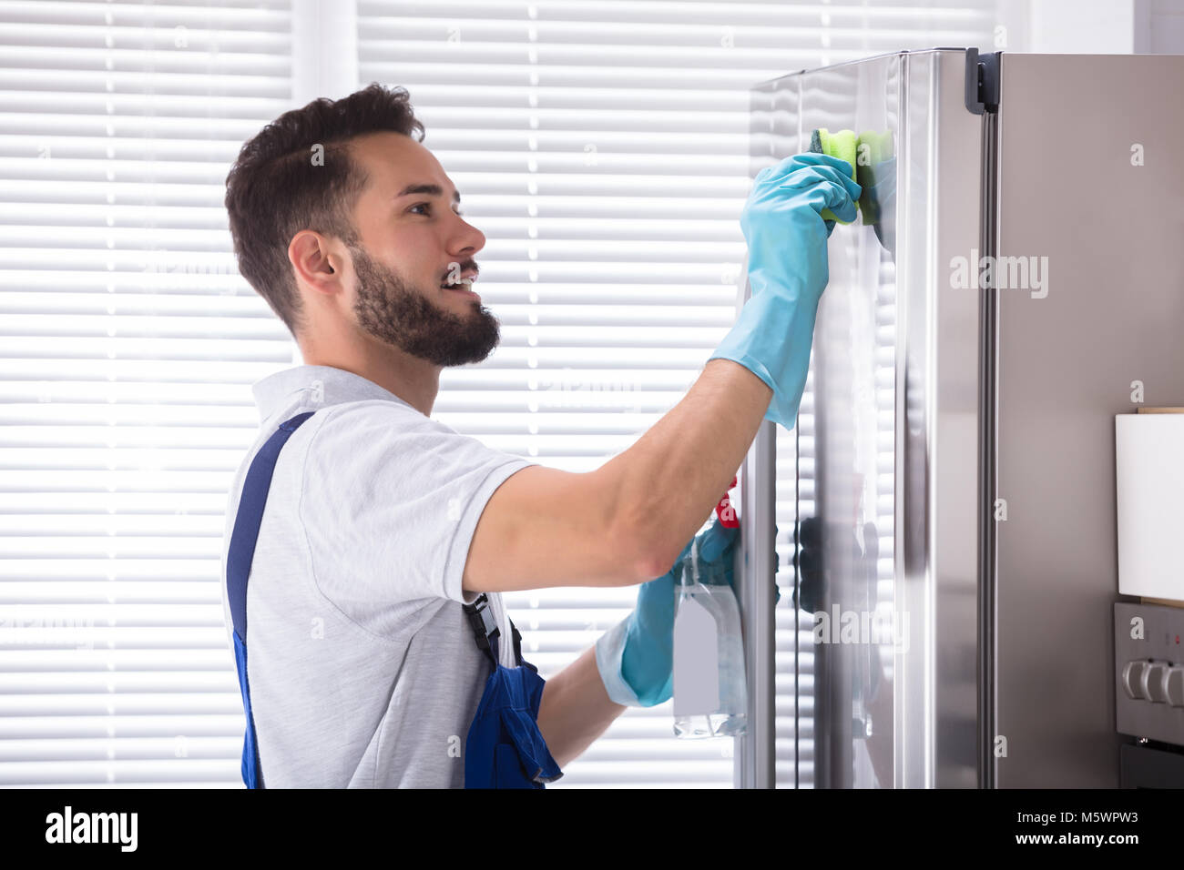 Side View Of A Young Male Janitor Cleaning Refrigerator In Kitchen ...