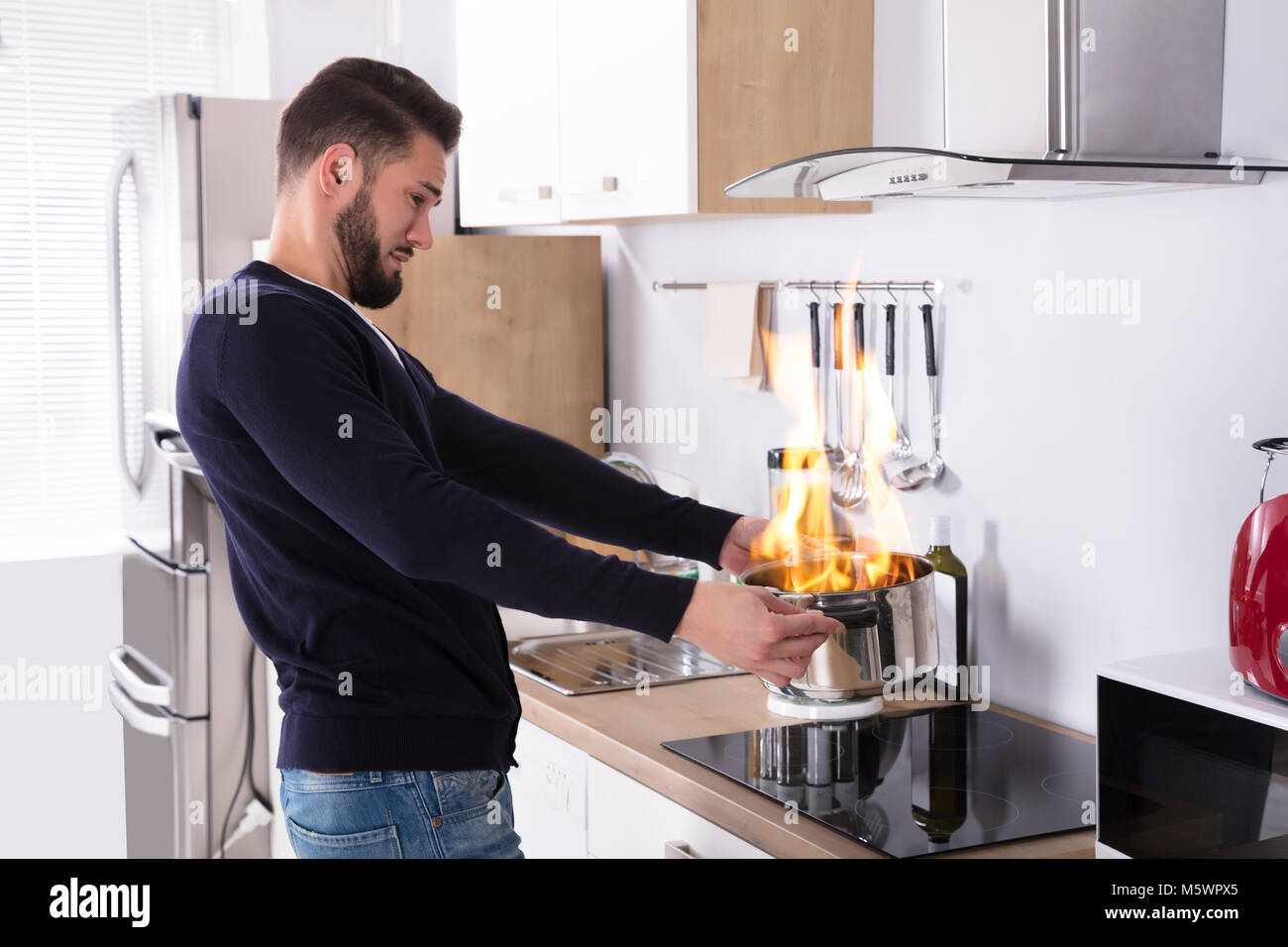 Side View Of A Young Man Holding Utensil On Fire In Kitchen Stock Photo ...