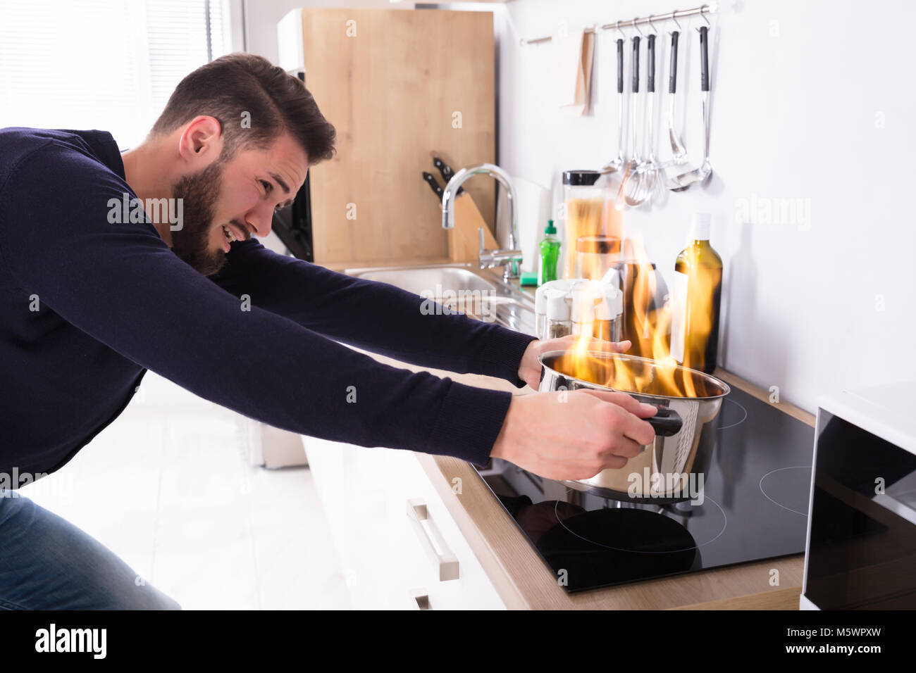 Side View Of A Young Man Holding Utensil On Fire In Kitchen Stock Photo ...