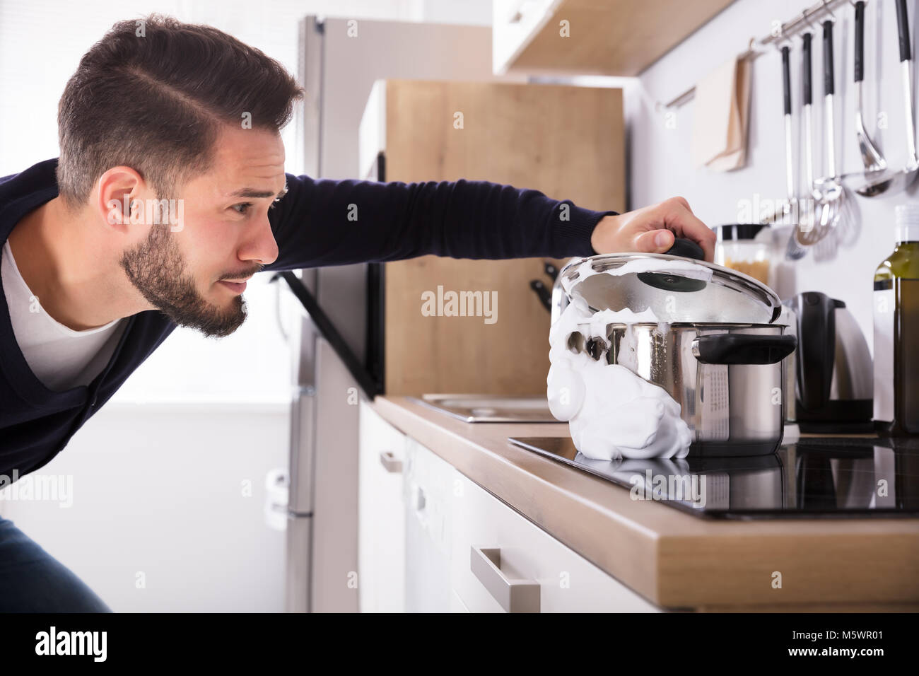Sad Young Man Looking At Spilling Out Boiled Milk From Utensil On ...