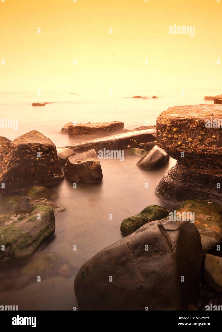 Image of the sea with rocks in foreground at sunset with long exposure ...