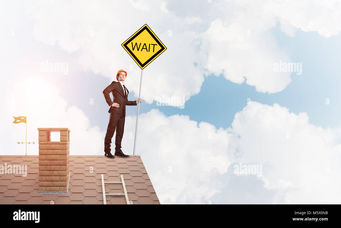 Young businessman on house brick roof holding yellow signboard. Mixed ...