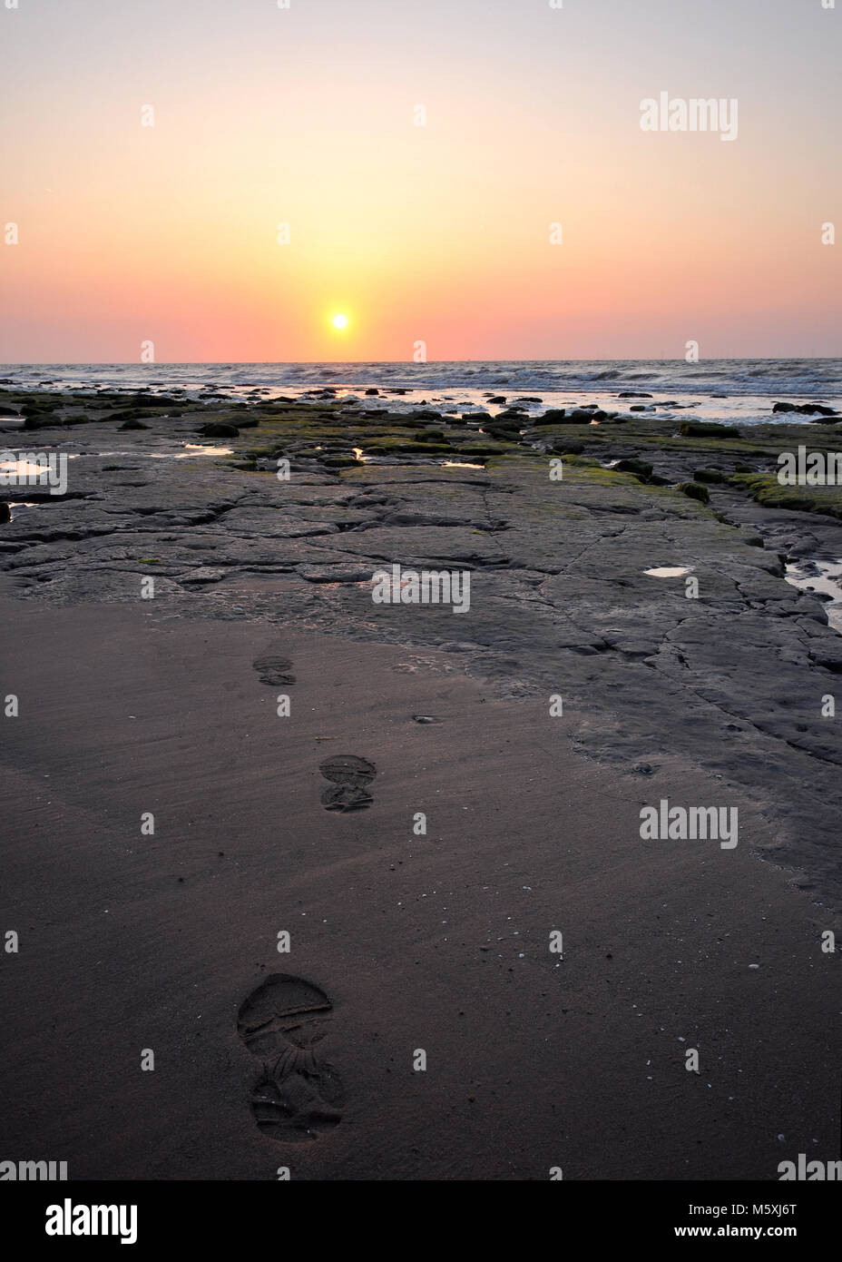 Beach picture with sand, rocks and footprints leading to a Sunset ...