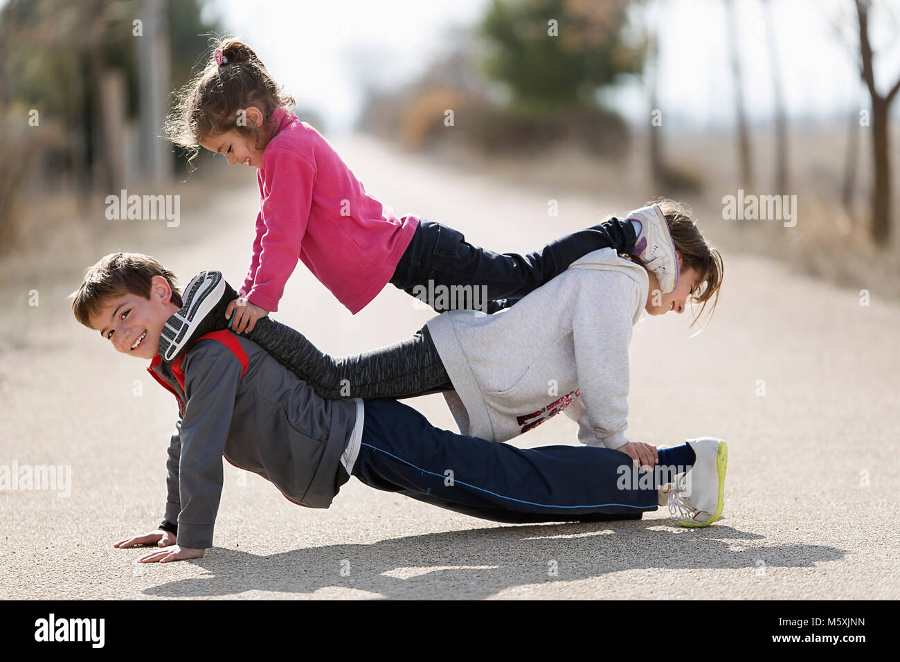 Three children lying on the floor on top of each other doing acrobatics ...