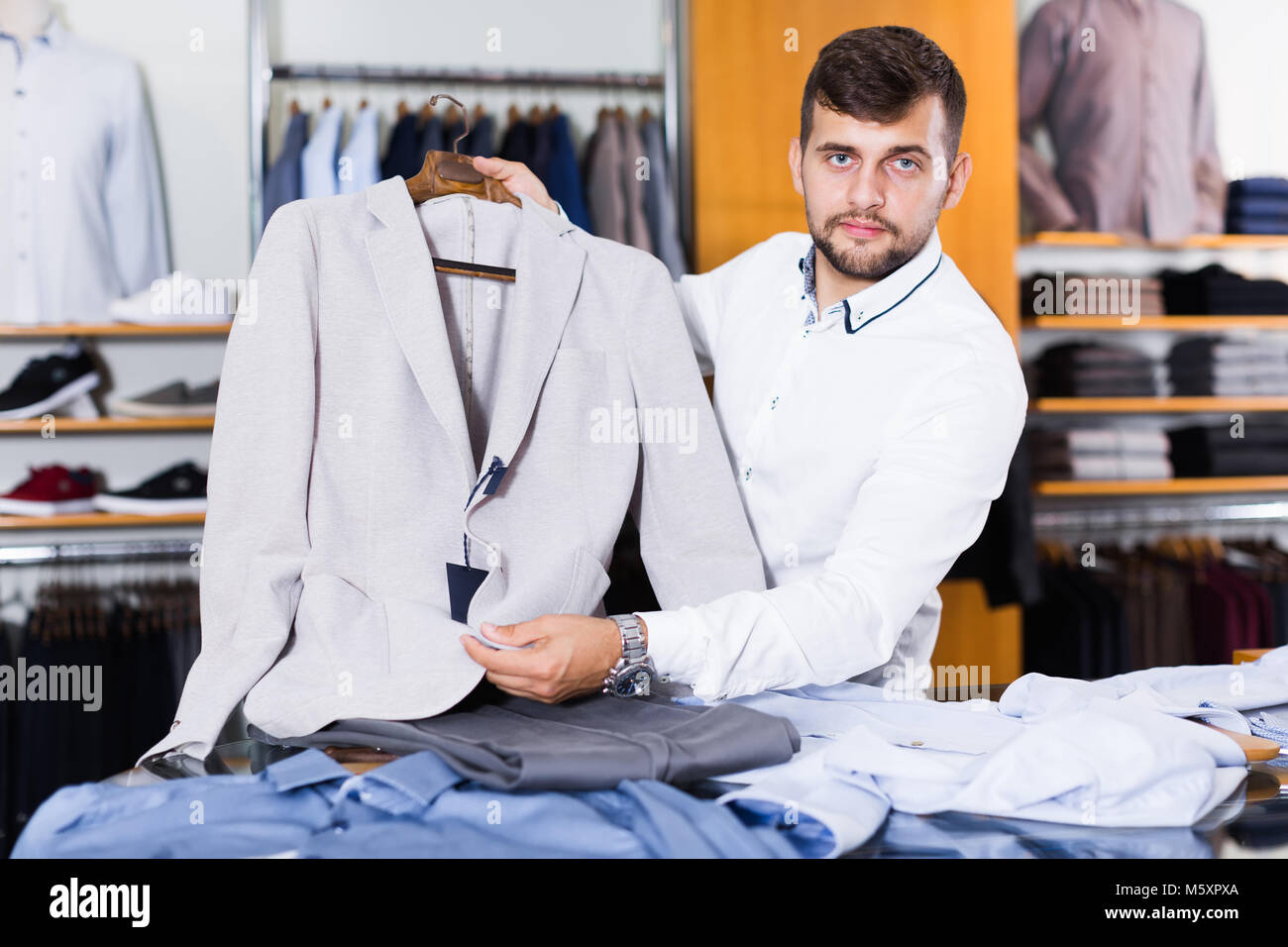 positive salesman displaying classic jacket in men clothes shop Stock ...