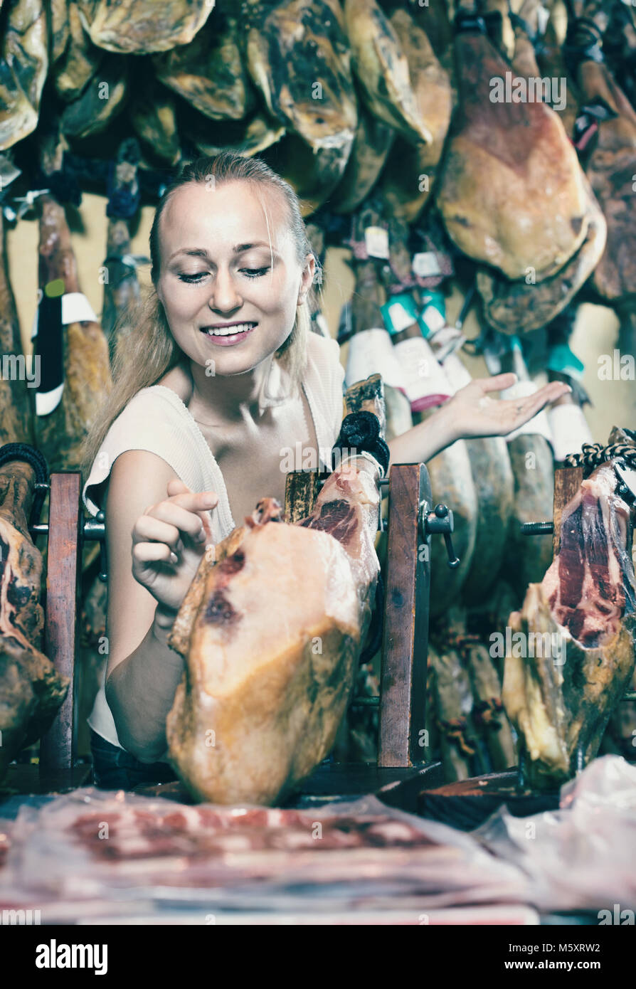 Positive cheerful young female customer choosing iberian ham in meat ...