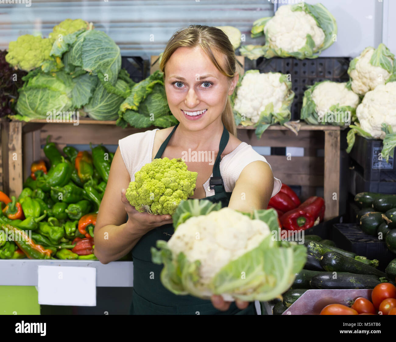 cheerful young female seller wearing apron holding fresh cabbage on ...