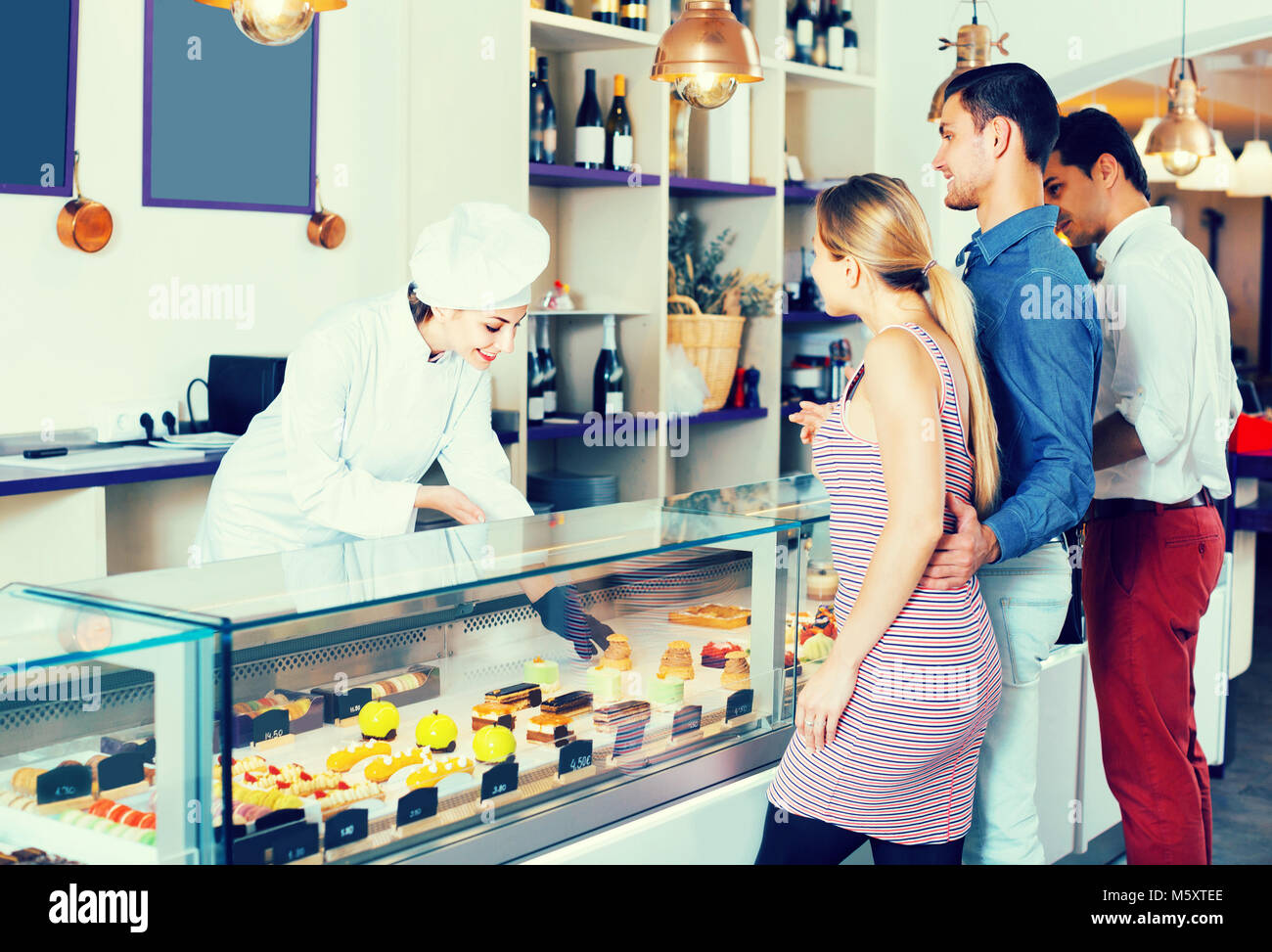 Positive pastry chef female is serving cakes from showcase in pastry ...