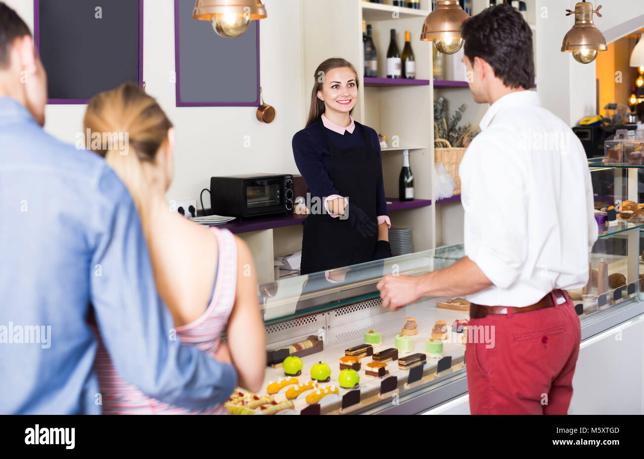 Female confectioner helping customers to choose sweets in comfortable ...