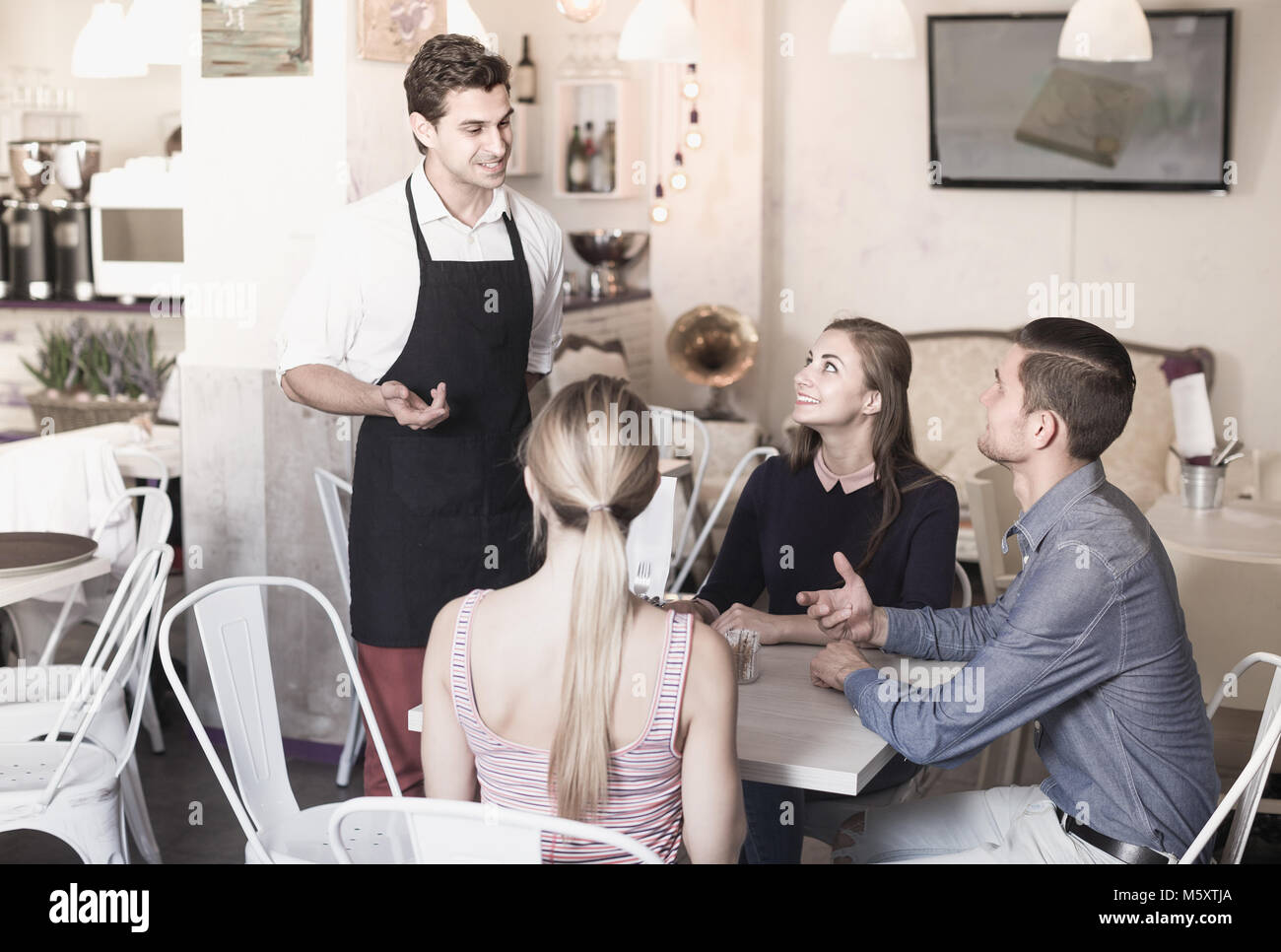 Adult waiter is greeting visitors in cafe and taking order Stock Photo ...