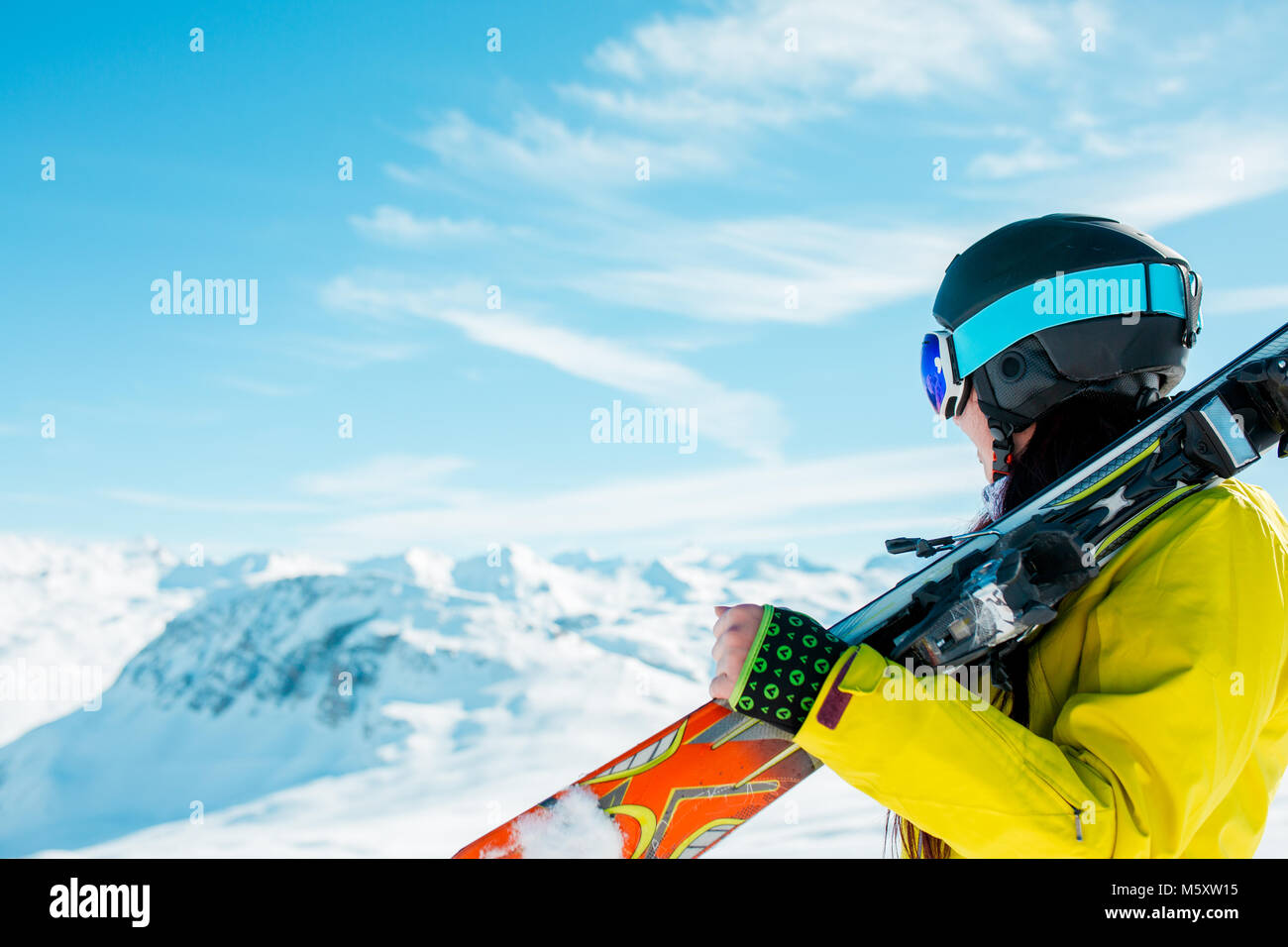Side view of sporty woman in helmet with skis on her shoulder against ...