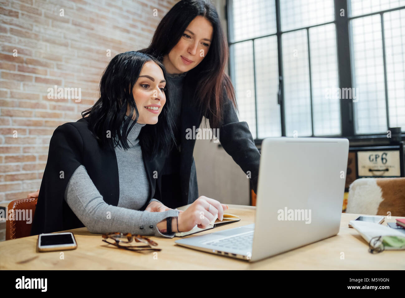 Two young women indoor using laptop computer - remote working, business ...