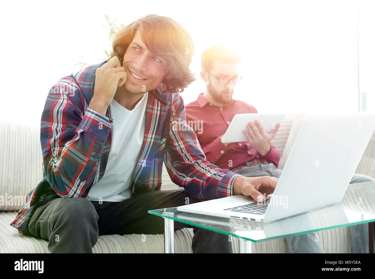 two guys sitting on the couch, talking on the smartphone and ...