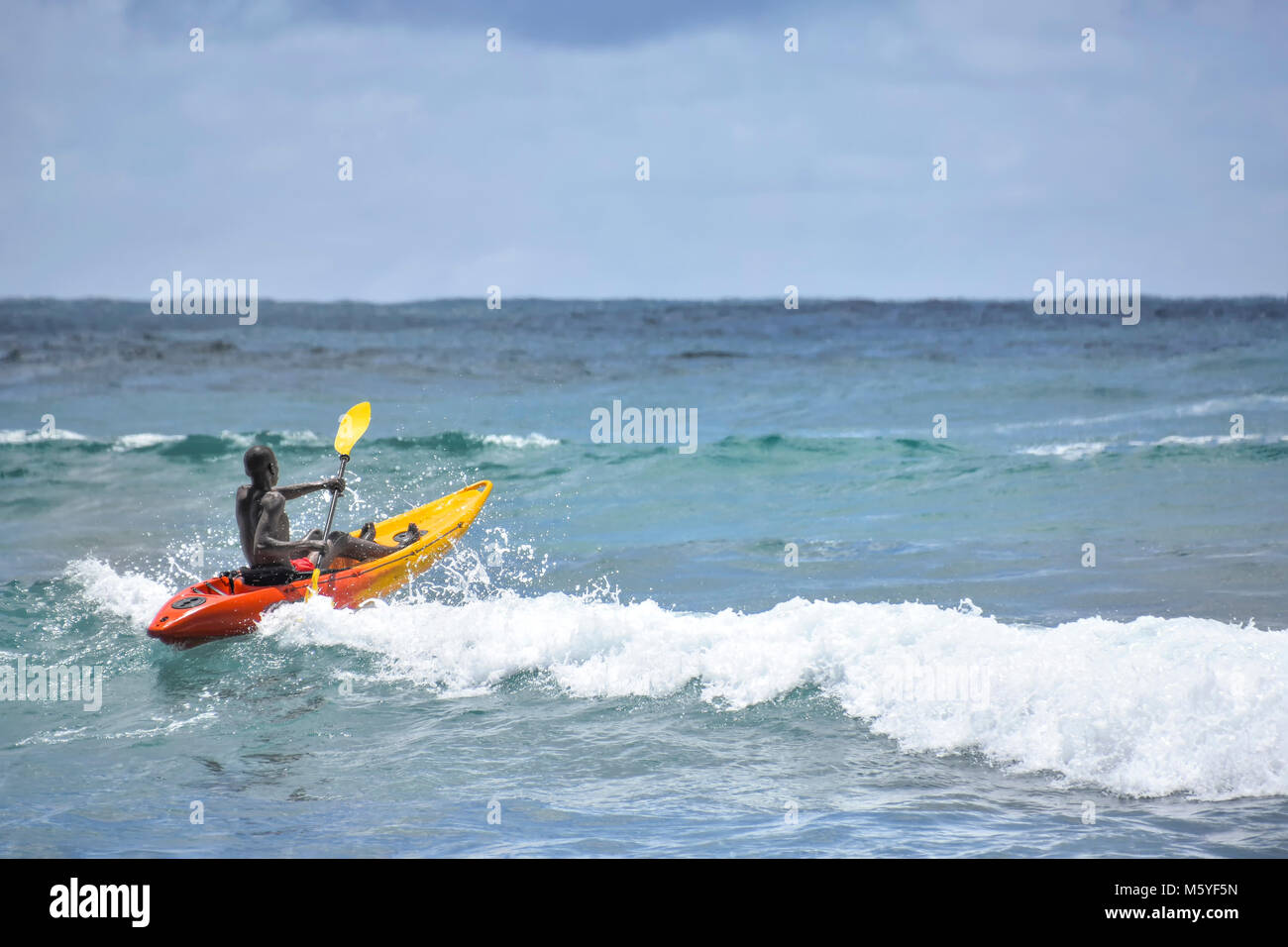A lifeguard in a red and yellow kayak on patrol peddling on a sunny day ...