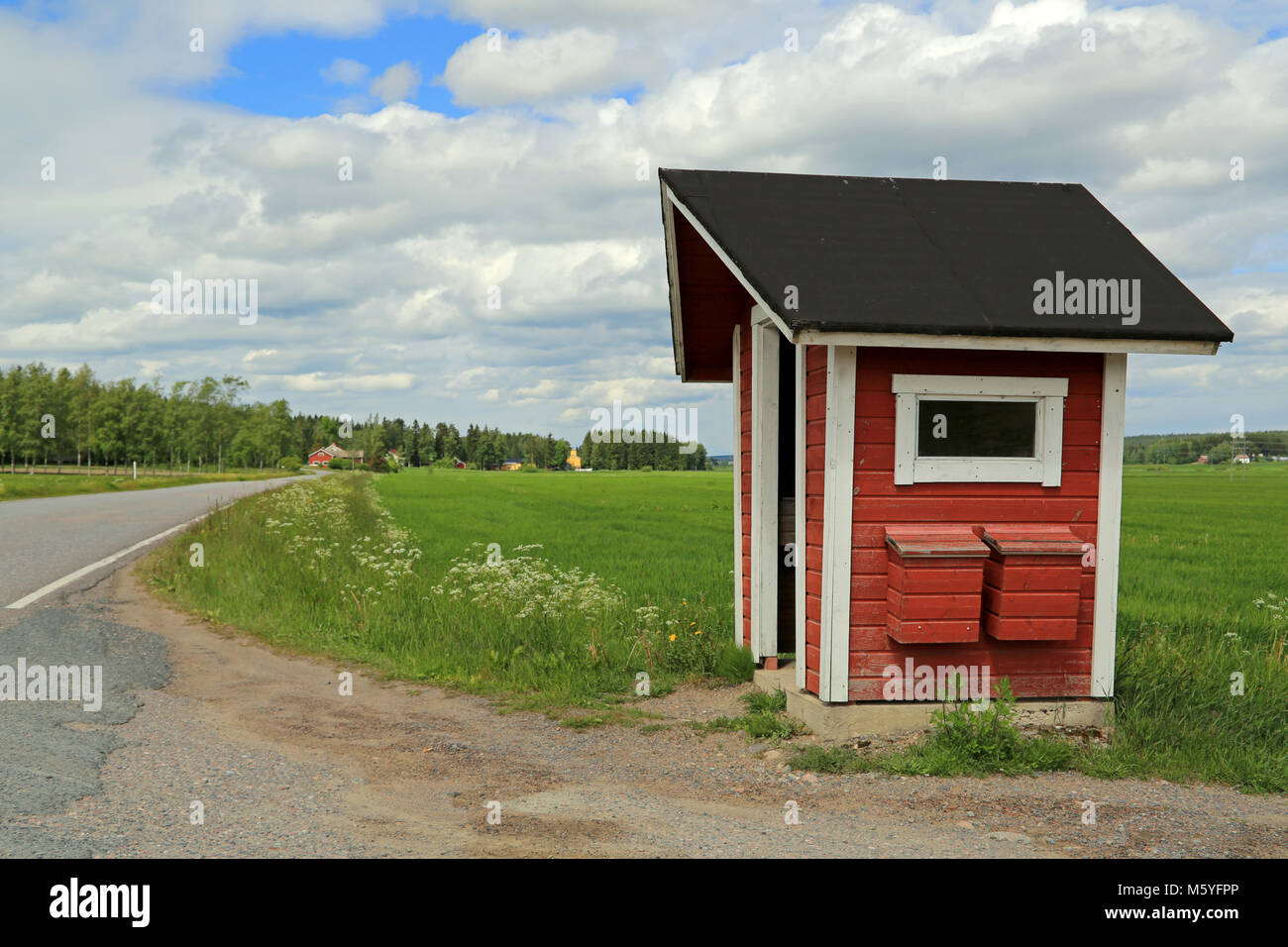 Red wooden bus stop shelter and two mail boxes by rural road at summer ...