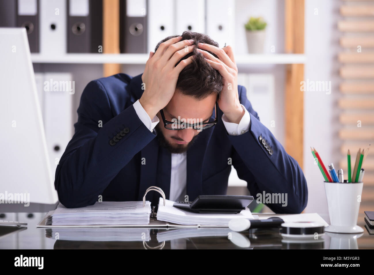 Young Man Suffering From Headache Working In Office With Bill Over Desk ...