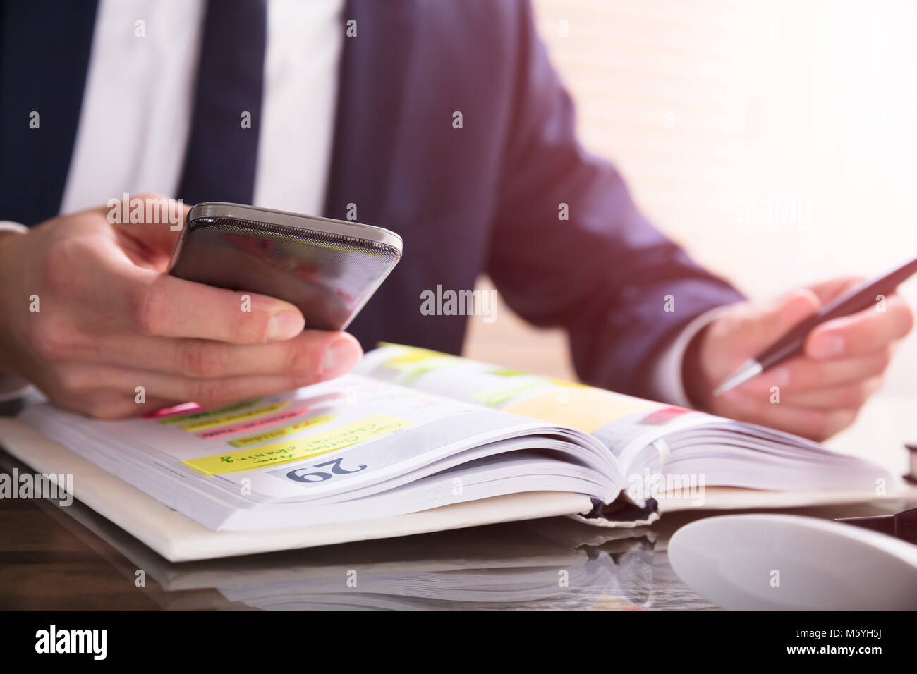 Businessperson Using Mobile Phone With Diary On Desk Stock Photo - Alamy