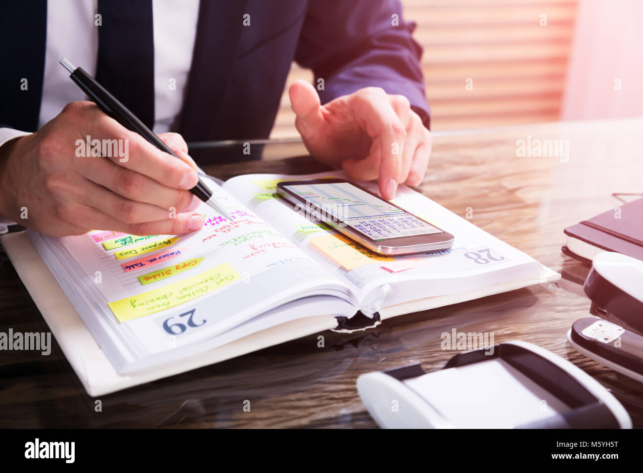 Businessperson Using Mobile Phone With Diary On Desk Stock Photo - Alamy