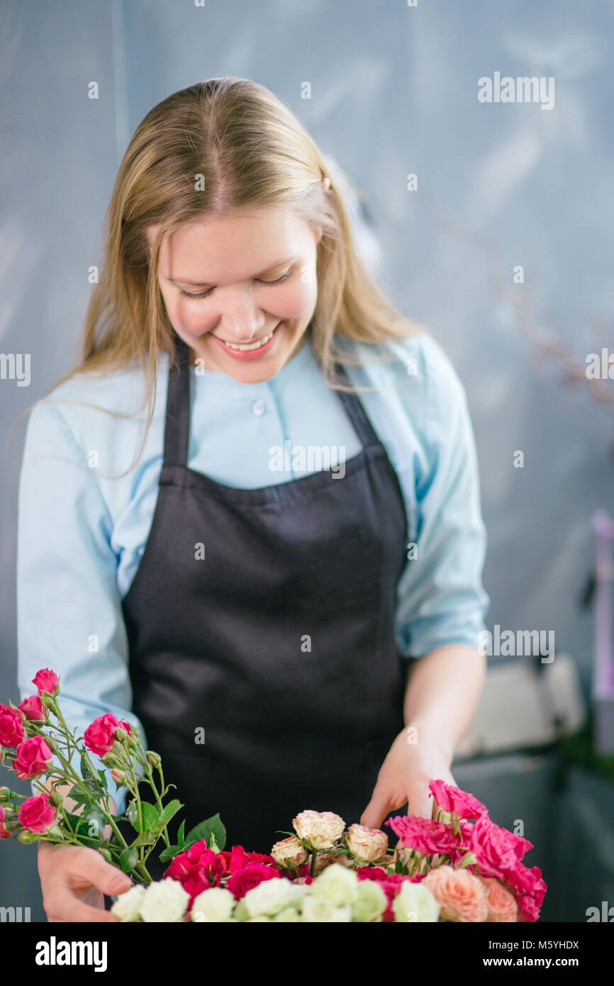 young shop assistant smiling and looking at made bounch of flowers at ...