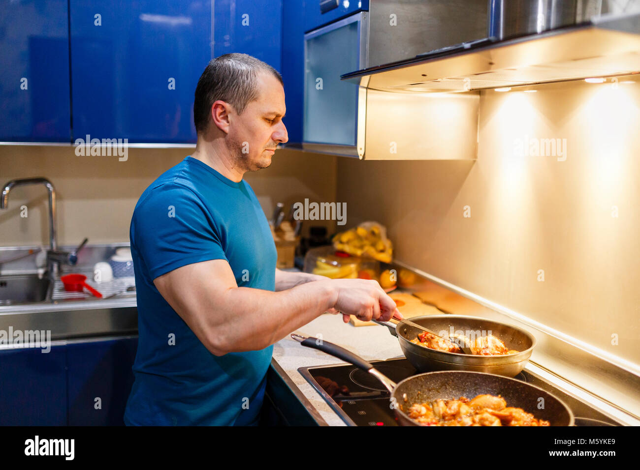 The man in the kitchen is cooking at home at the wok Stock Photo - Alamy