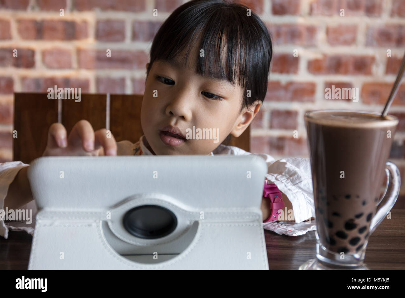 Asian Chinese little girl playing tablet computer at indoor cafe Stock ...