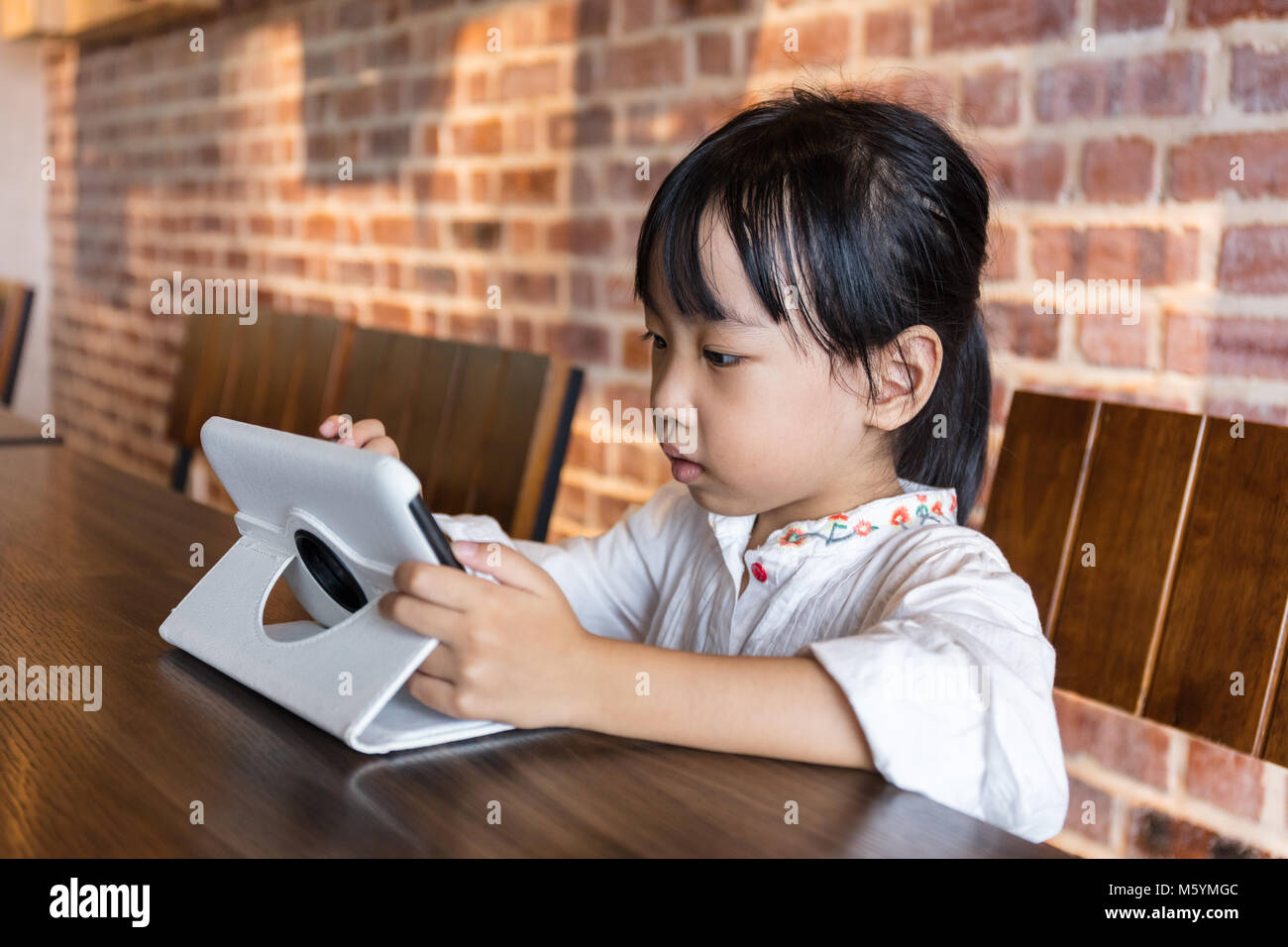 Asian Chinese little girl playing tablet computer at indoor cafe Stock ...
