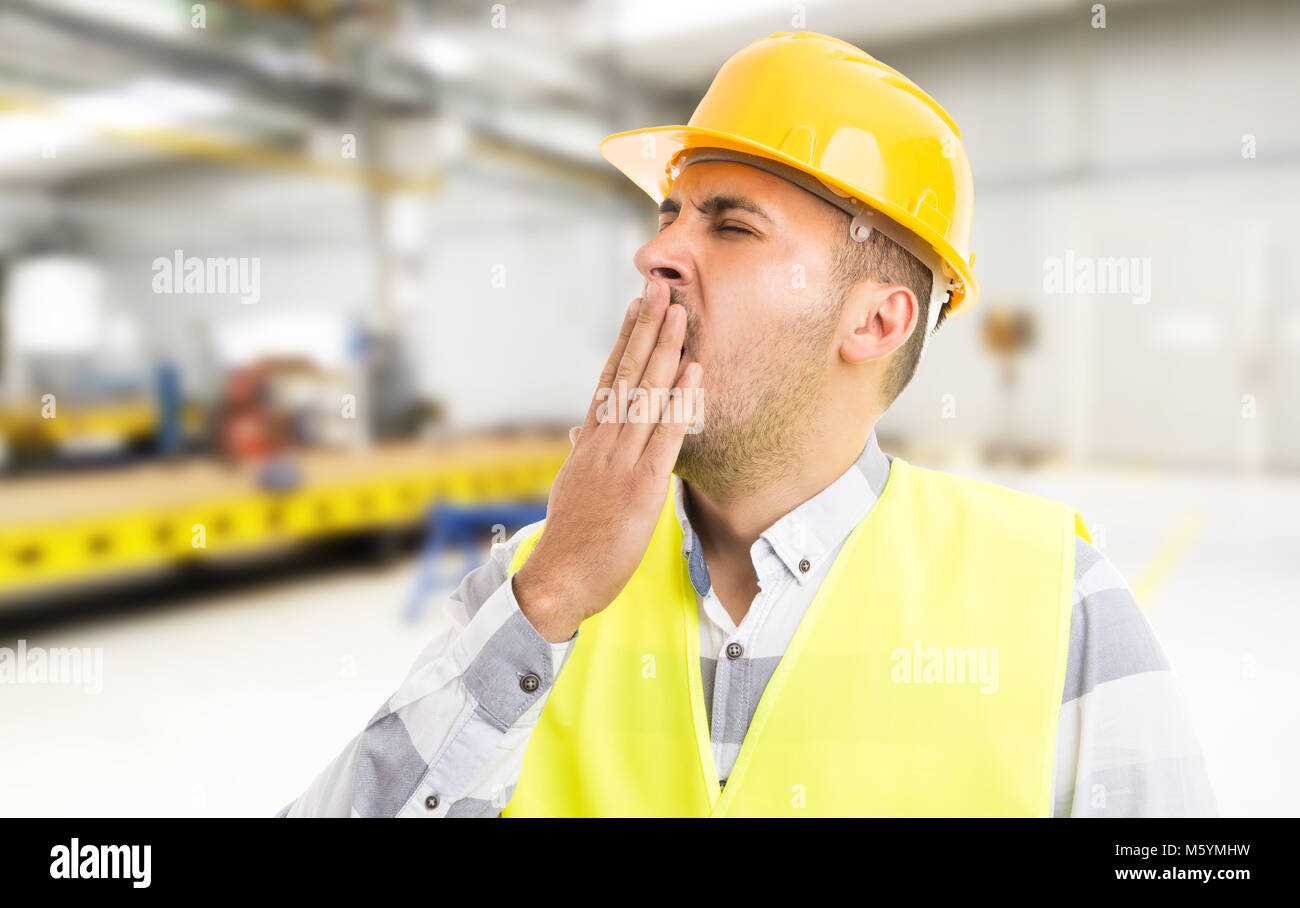 Tired workman yawning sleepy on workplace inside factory background ...