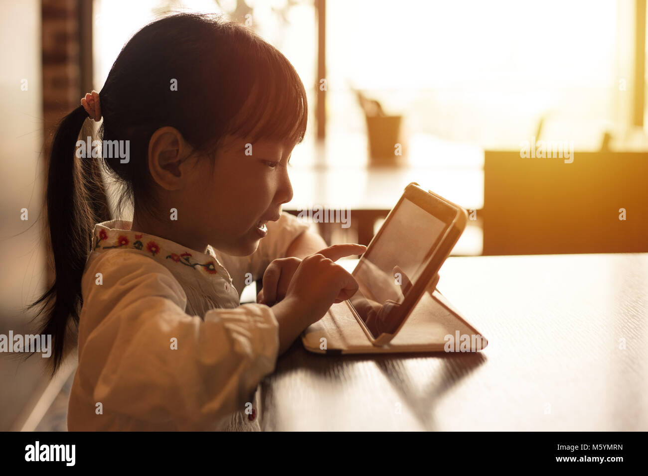 Asian Chinese little girl playing tablet computer at indoor cafe Stock ...