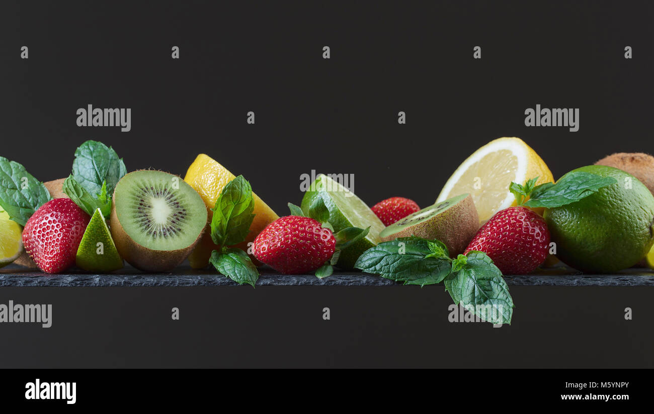 Different juicy fruits and mint leaves on black background. Copy space ...