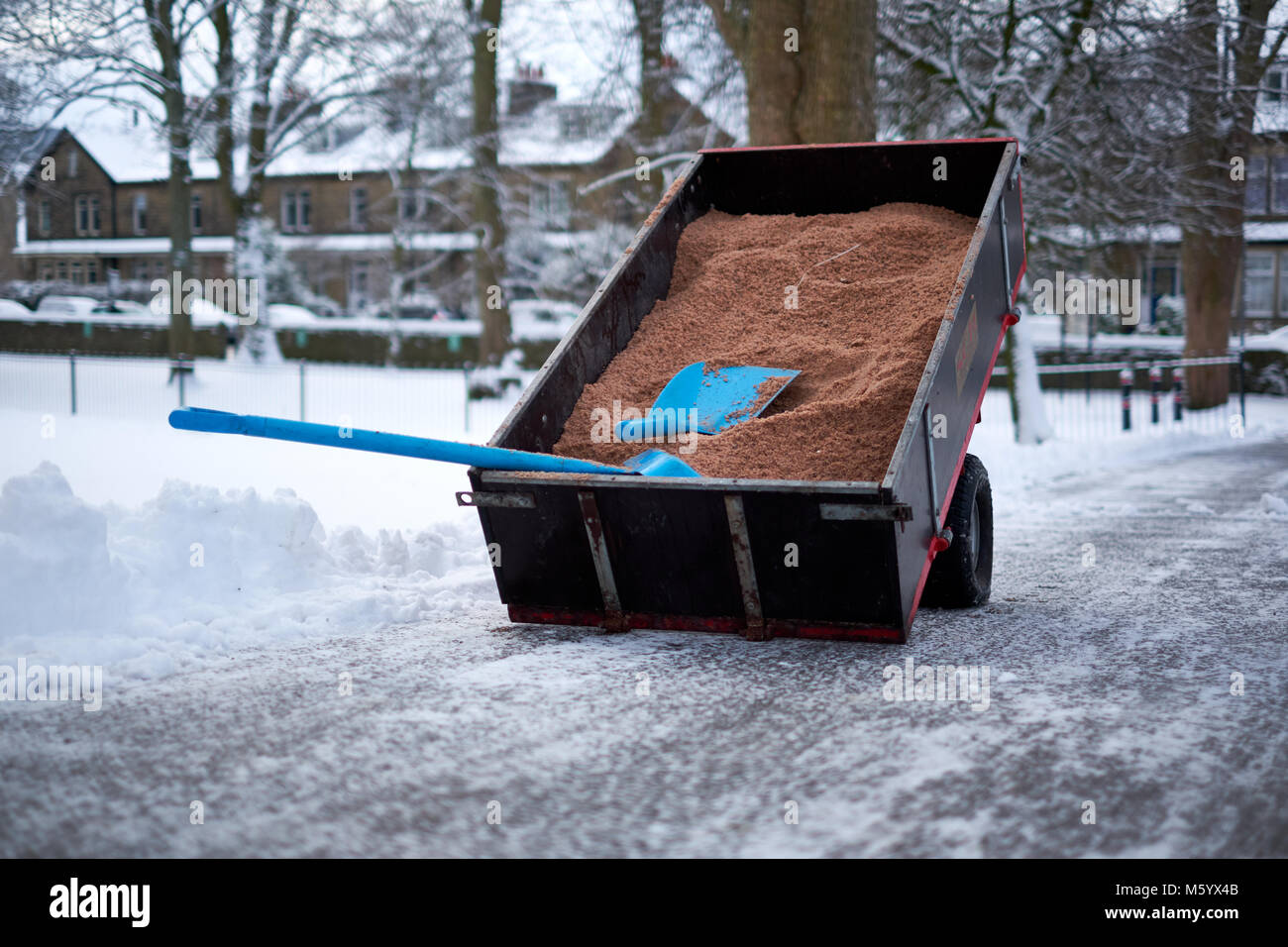A trailer of grit with a blue spade and shovel sits on a driveway ...