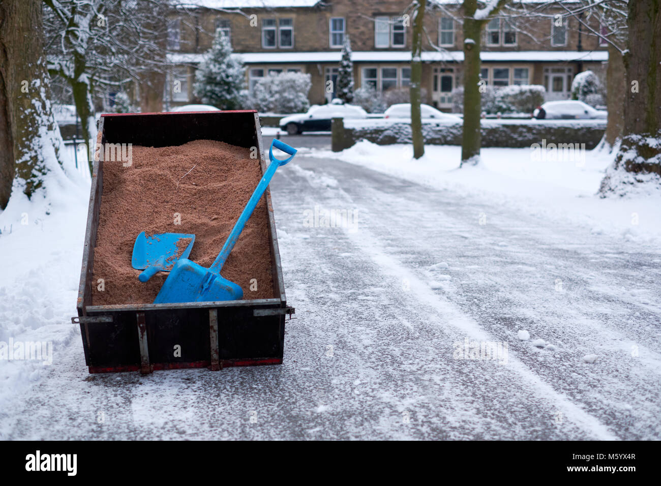 A trailer of grit with a blue spade and shovel sits on a driveway ...