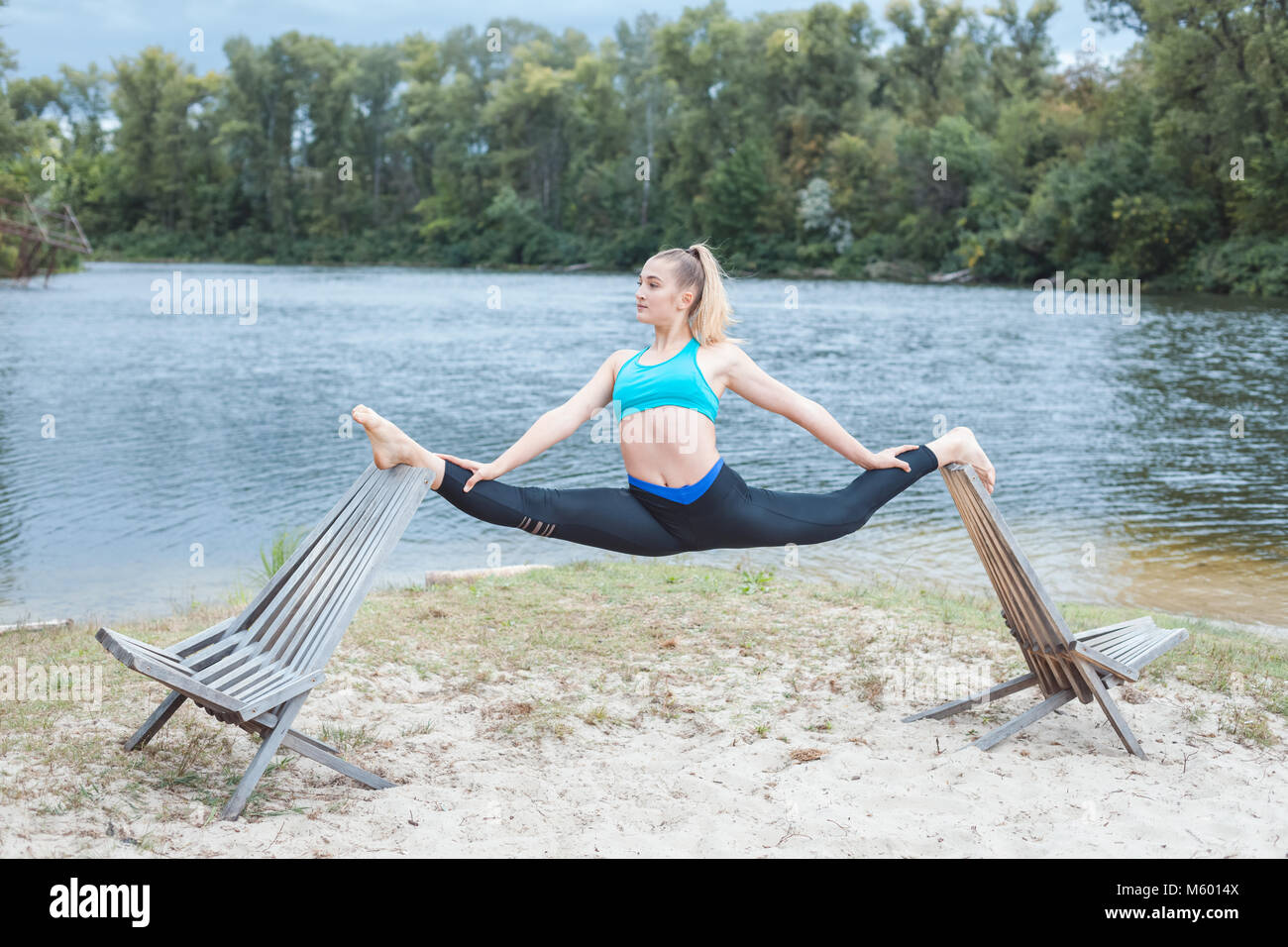 Girl is doing sports near the lake. She does the splits on sunbeds ...