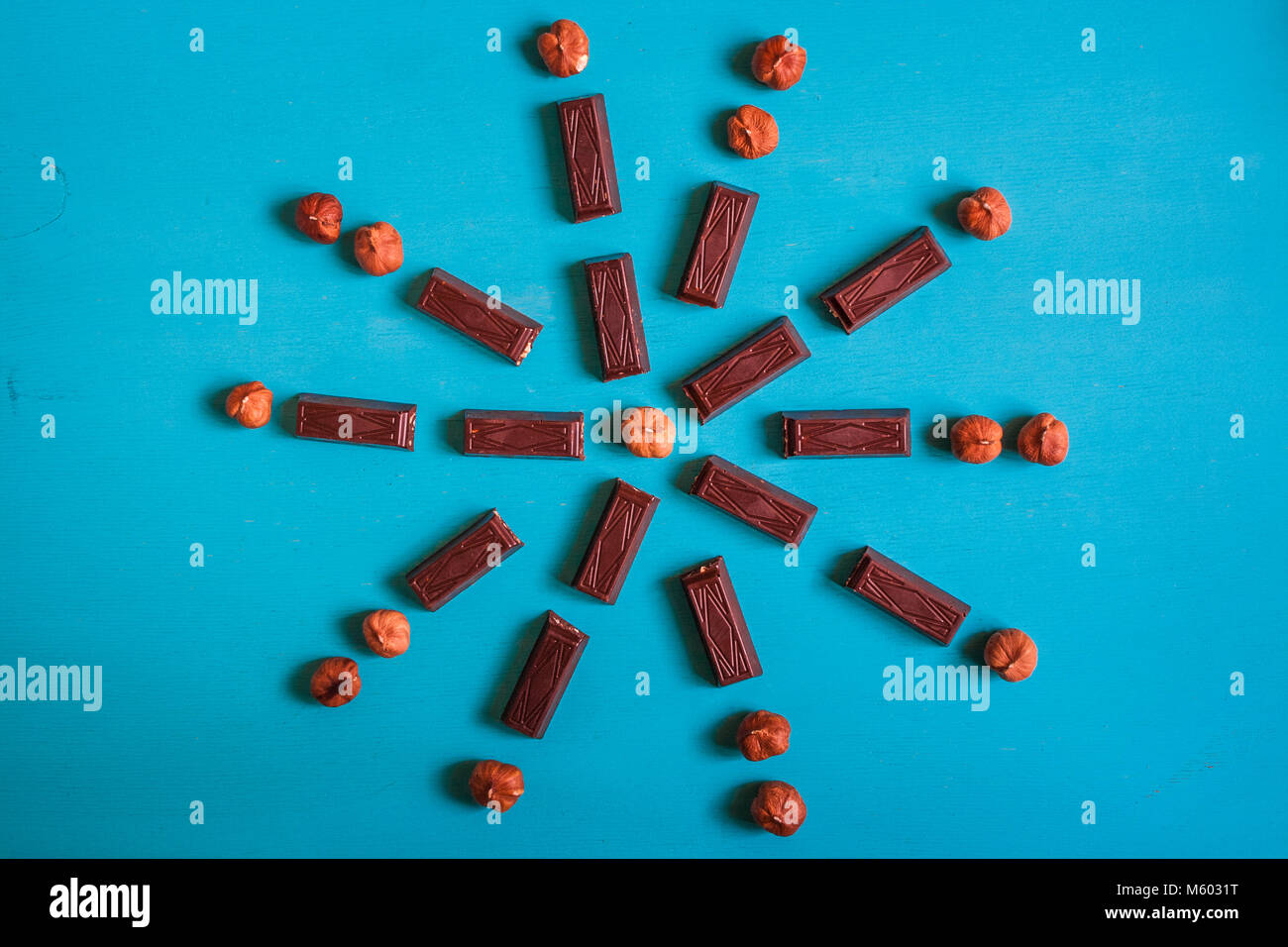 Radial flat lay rectangular pieces of chocolate and hazelnuts on blue ...
