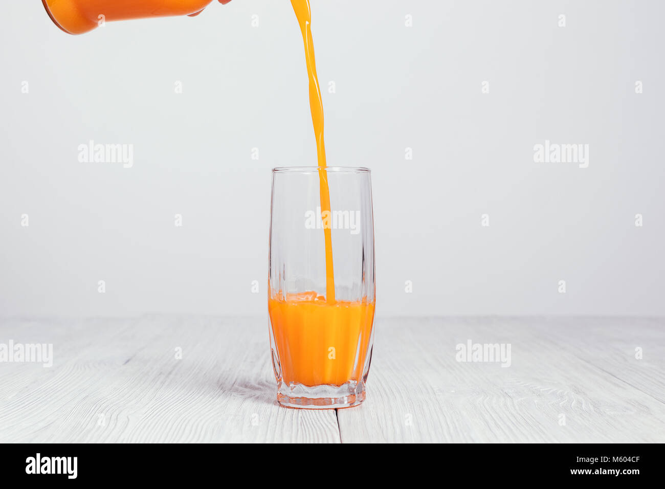 Orange juice is poured from a bottle into a glass on a white background ...