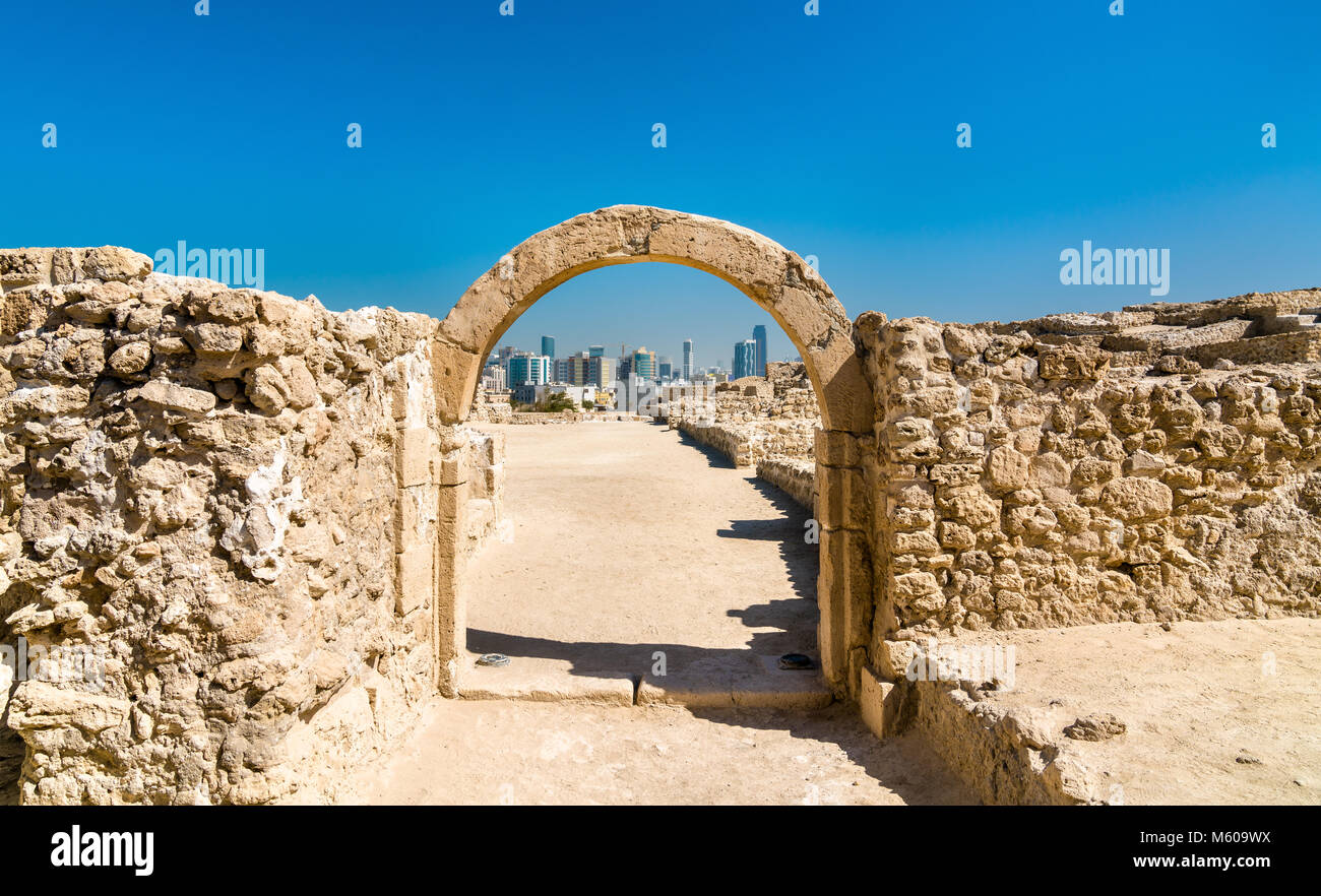 Ancient arch at Bahrain Fort with skyline of Manama. A UNESCO World ...