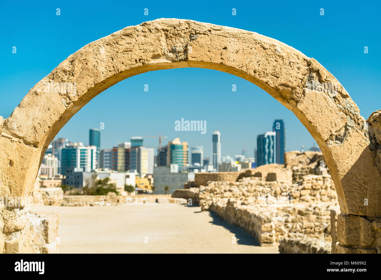Ancient arch at Bahrain Fort with skyline of Manama. A UNESCO World ...