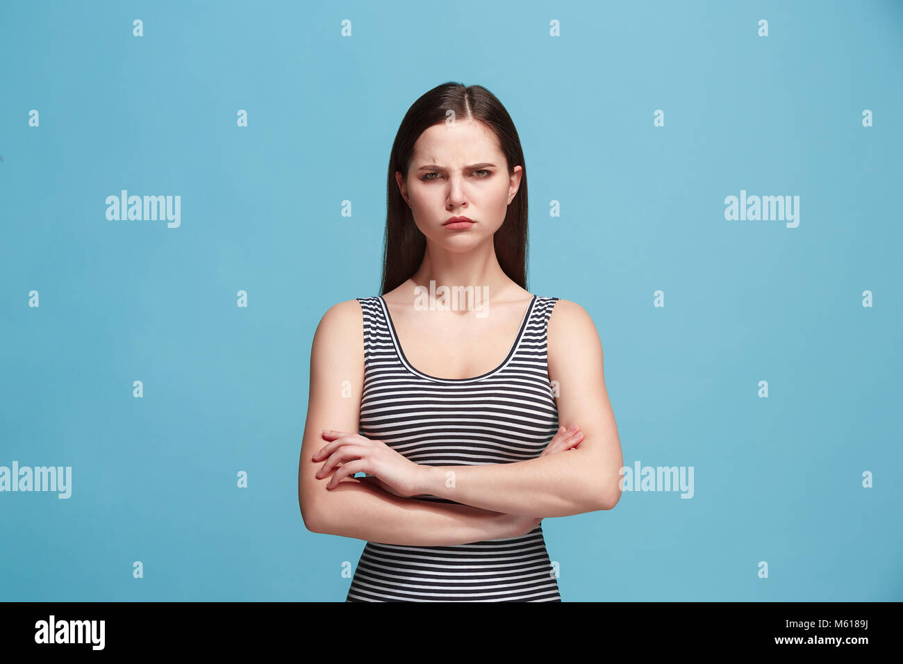 The serious woman standing and looking at camera against blue ...