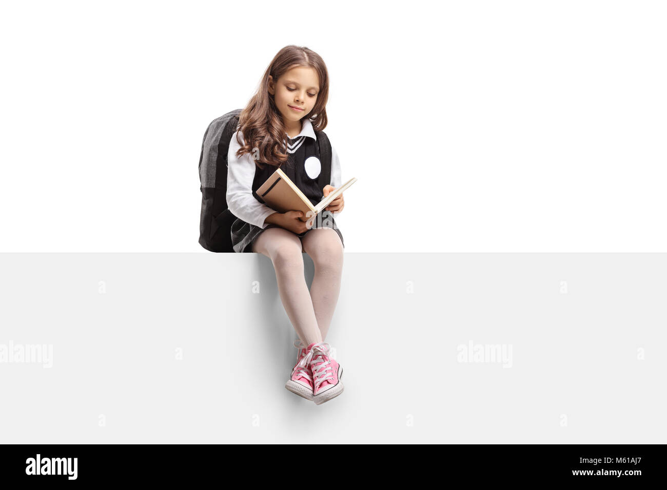 Schoolgirl seated on a panel reading a book isolated on white ...